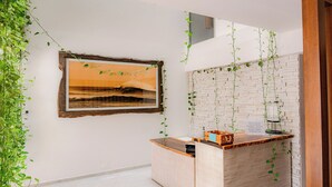 Uma área de recepção com balcão de madeira, um quadro na parede e plantas penduradas.