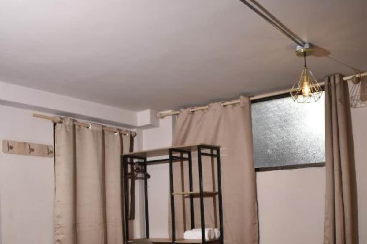 Quarto com cama, cadeira, escrivaninha e janela com cortinas.