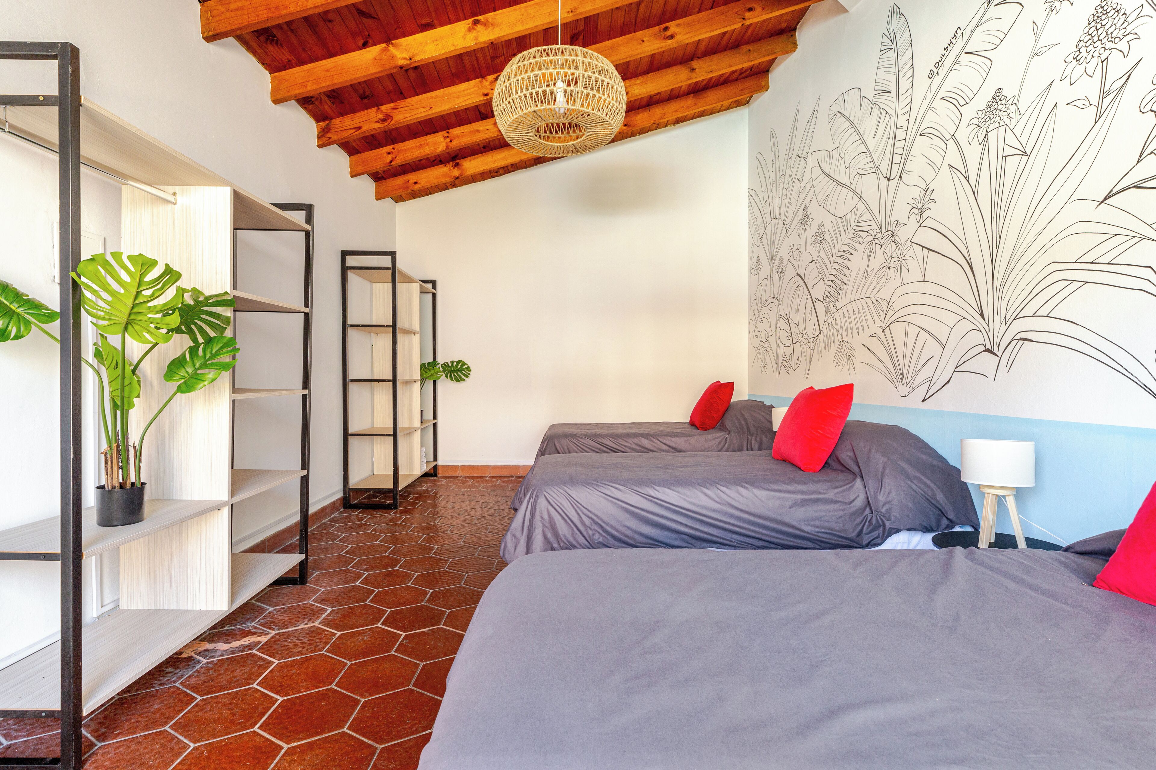 Quarto com duas camas, um grande mural na parede, luminária pendente e uma planta.