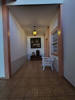 Um corredor com piso de azulejos, um banco, luminária fixada na parede e uma obra de arte emoldurada.