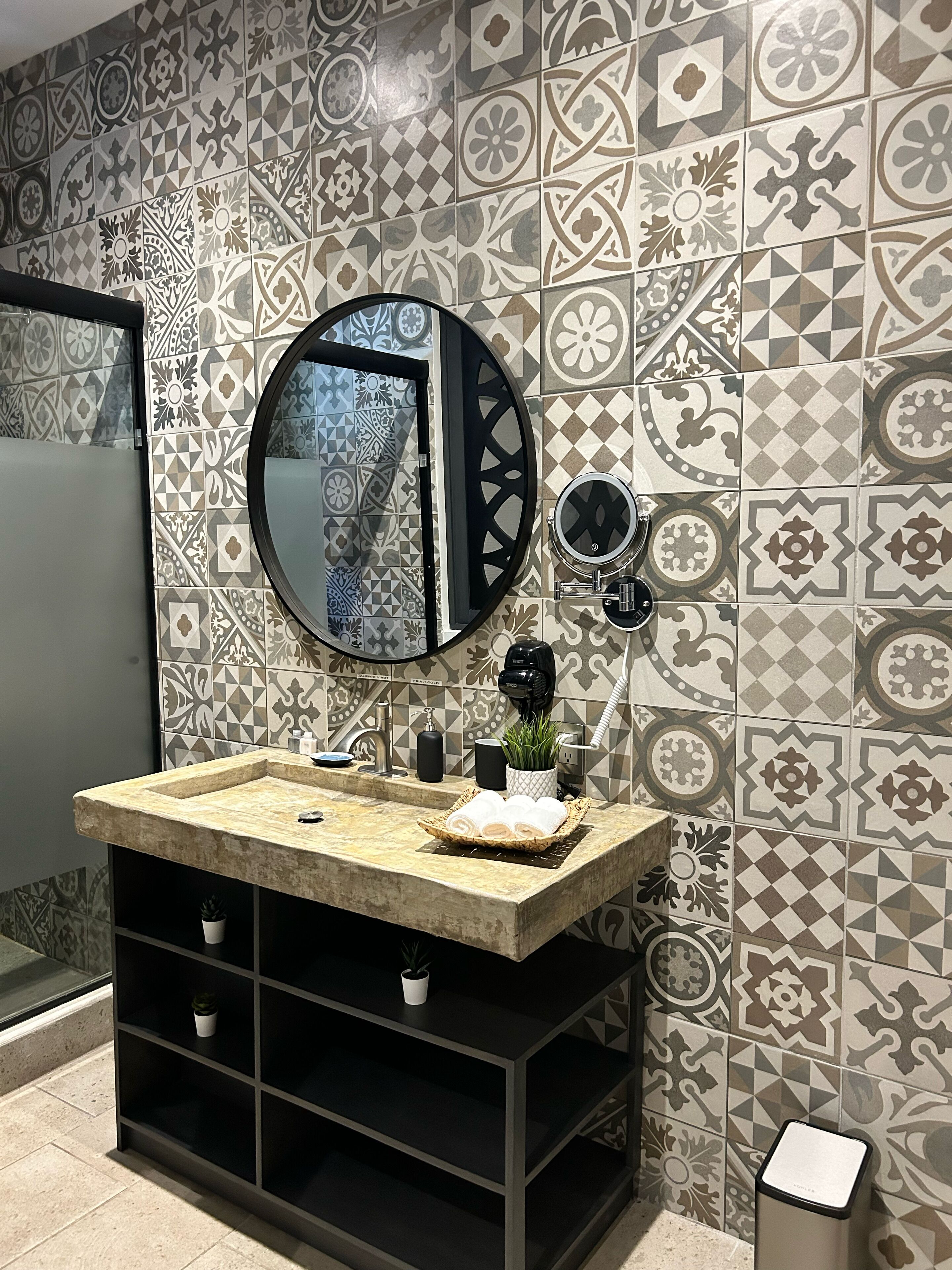 Casa de banho com lavatório, espelho redondo, secador de cabelo e lixeira.