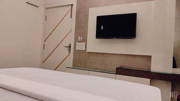 Quarto de hotel com cama, televisão fixada na parede e divisória de vidro.