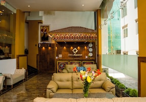 Um hall de entrada com balcão de recepção, um sofá com um vaso de flores e uma parede decorativa com relógios e um aviso.