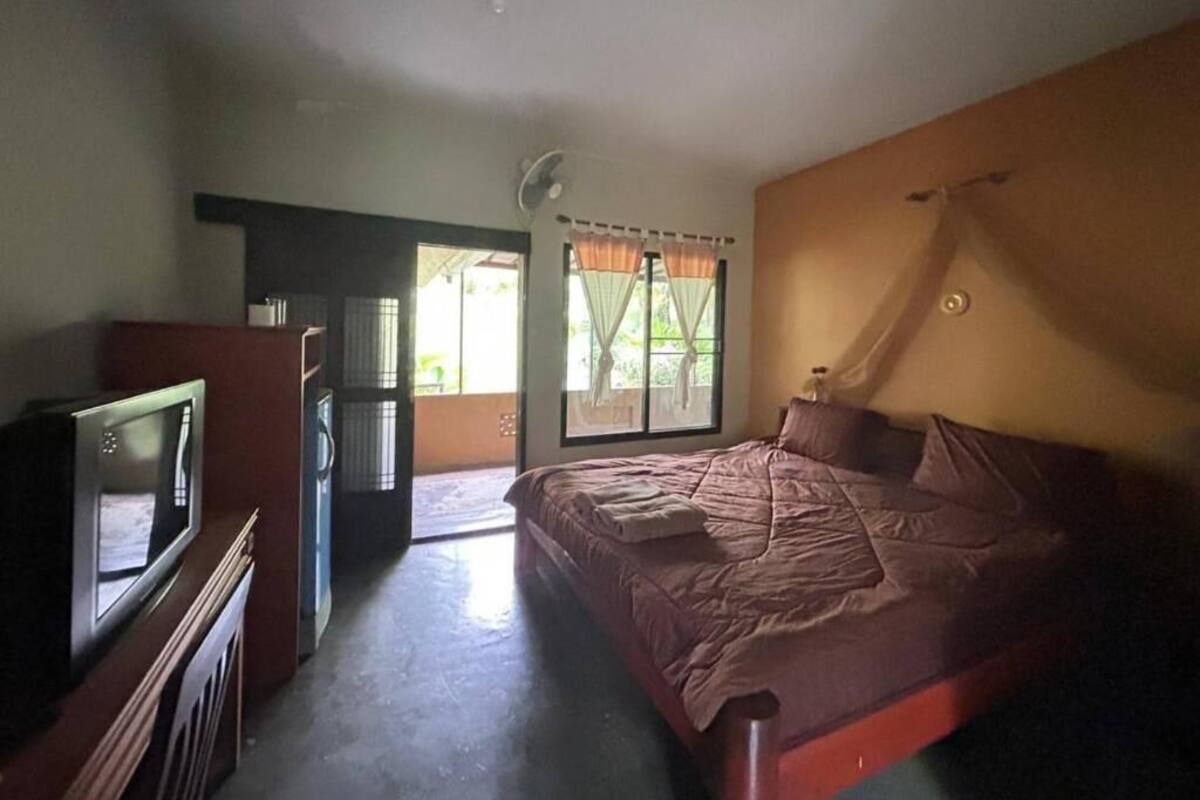 Quarto com cama, televisão, frigorífico e janela com cortinas.