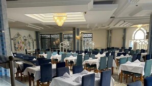 Uma sala de jantar ampla com piso de mármore, mesas organizadas com cadeiras azuis e arte decorativa nas paredes.