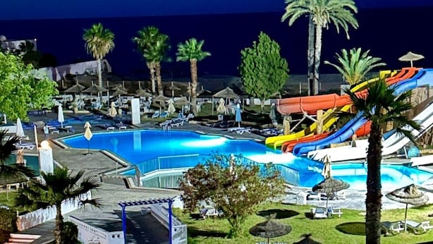 Uma área de piscina em resort com um toboágua, palmeiras e espreguiçadeiras.