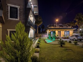 Um edifício moderno de vários andares com um jardim bem cuidado e um carro estacionado em frente.