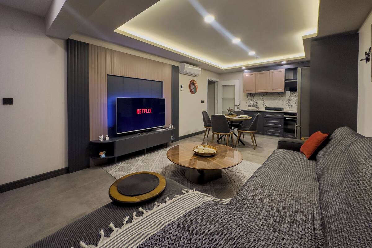 Uma sala de estar moderna com uma televisão de tela plana, um sofá, uma mesa de centro e um espaço de jantar com cadeiras.