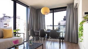 Uma sala de estar moderna com sofá, mesa de jantar, cadeiras e uma janela grande com cortinas.