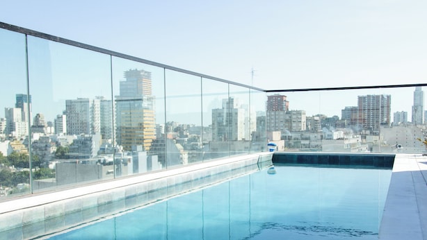 Piscina no terraço com vista para a cidade, céu claro e arquitetura moderna.