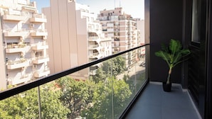 Uma varanda com um vaso de planta, guarda-corpo de vidro e vista para edifícios altos.