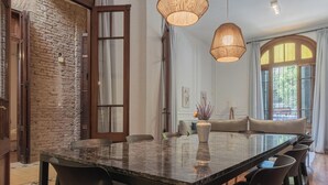 Uma sala de jantar com uma grande mesa de mármore, várias cadeiras, um vaso com flores e uma parede de tijolos.