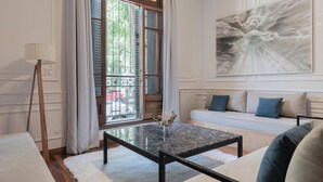 Uma sala de estar moderna com uma mesa de centro de mármore, um sofá com almofadas, um quadro abstrato grande e vista pela janela com persianas.