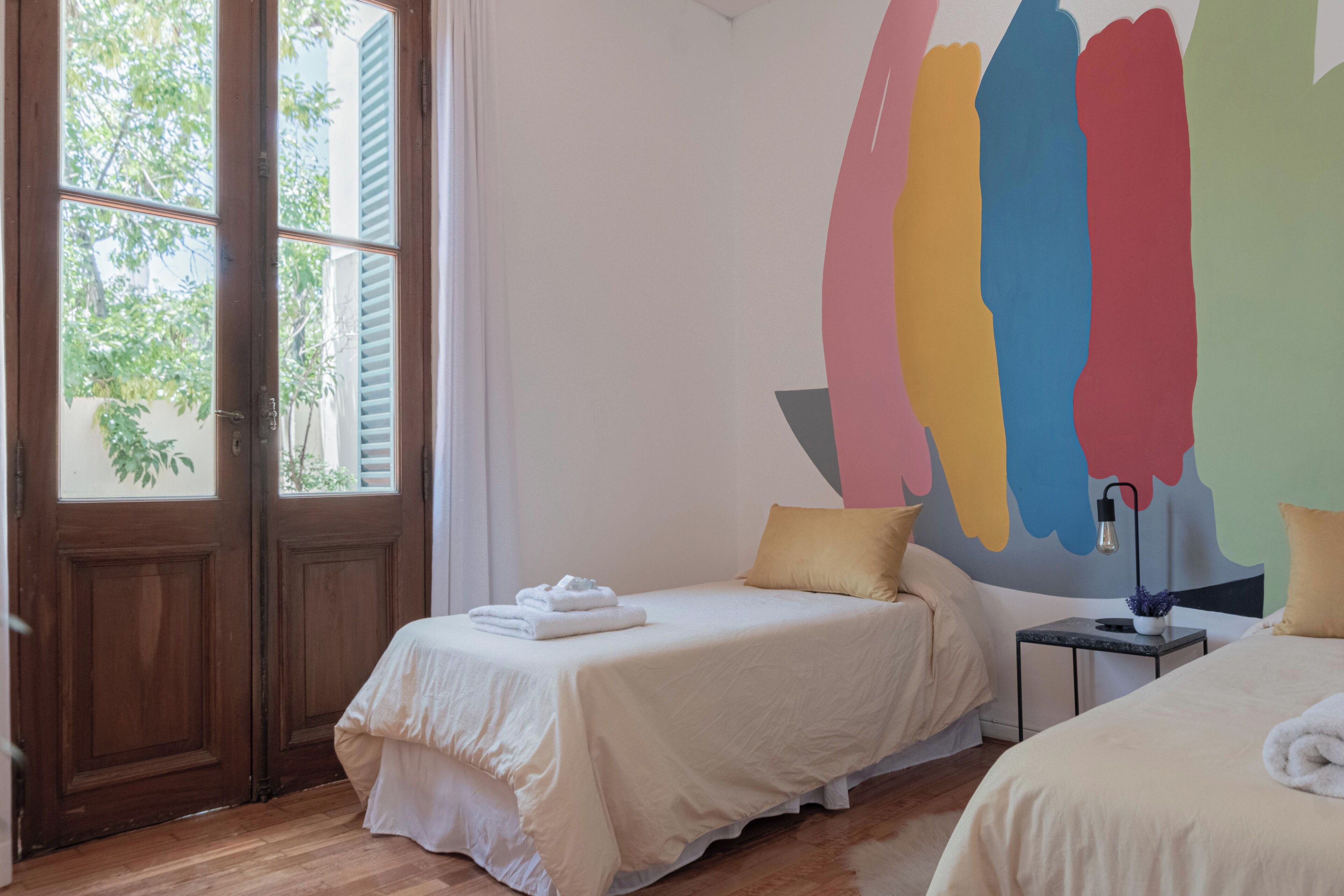 Quarto com duas camas, uma porta de madeira e uma janela grande.