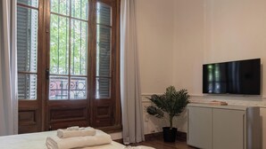 Quarto de hotel com cama, televisão, planta em vaso e minibar.