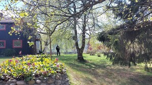 Uma casa de madeira rústica com telhado vermelho e detalhes brancos, rodeada por um jardim bem cuidado com plantas floridas e um muro de pedra.