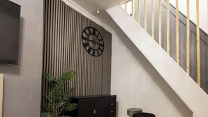 Uma sala de estar moderna com escada de madeira, um armário preto, uma planta em vaso e um relógio redondo na parede.