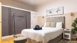 Um quarto com cama, mesas de cabeceira, um guarda-roupa cinzento e uma obra de arte na parede.