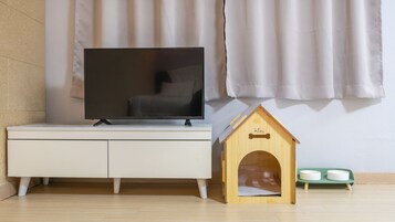 Uma televisão sobre um armário branco, uma casinha de cachorro de madeira e um comedouro verde para animais de estimação.