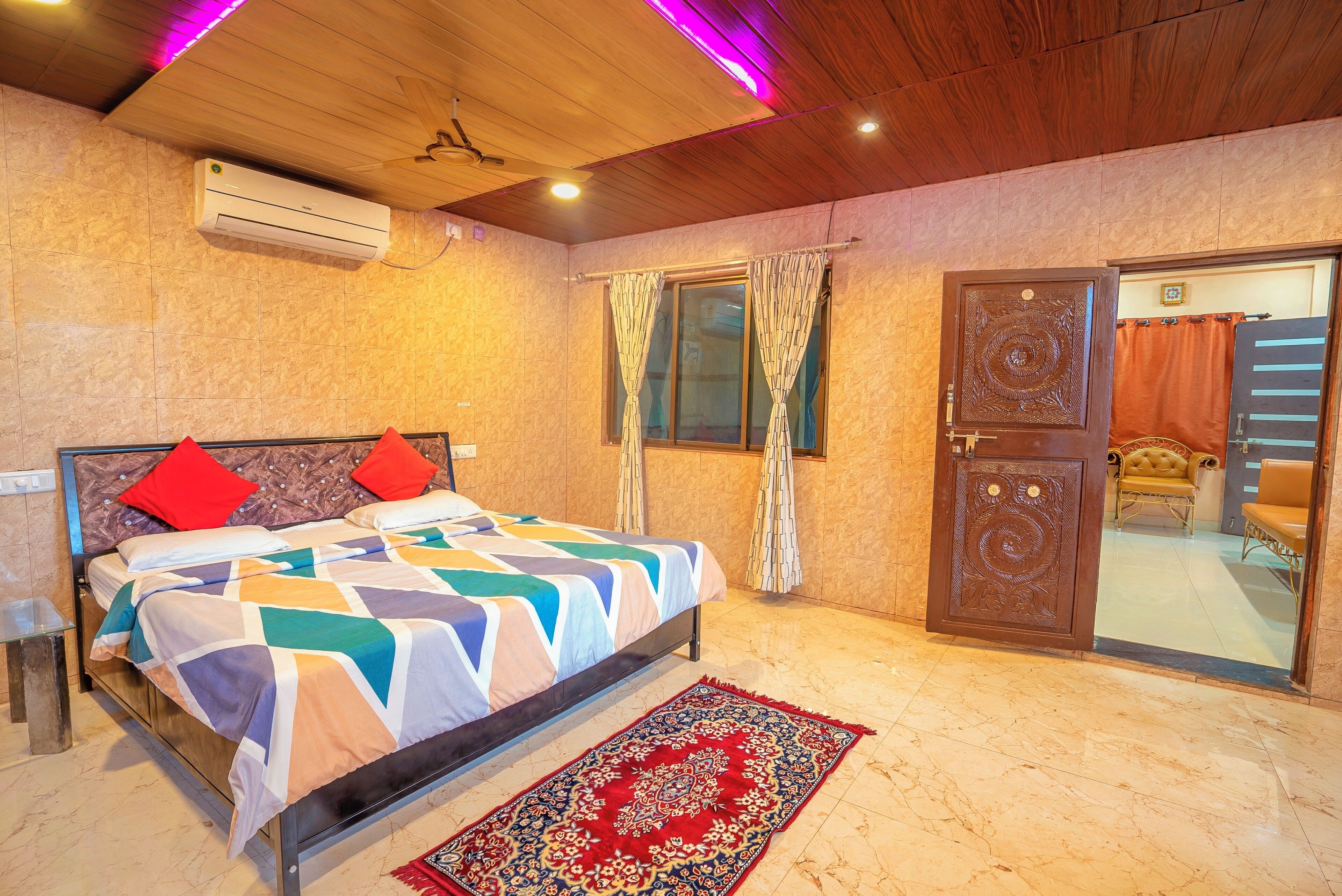 Quarto com cama, colcha estampada em vermelho e azul, teto de madeira, ar condicionado e tapete estampado em vermelho.