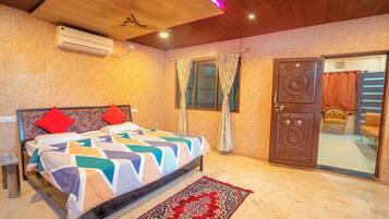 Quarto com cama, colcha estampada em vermelho e azul, teto de madeira, ar condicionado e tapete estampado em vermelho.
