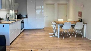 Uma cozinha moderna com armários brancos, uma mesa de jantar de madeira com quatro cadeiras e uma porta visível que dá para outro cômodo.