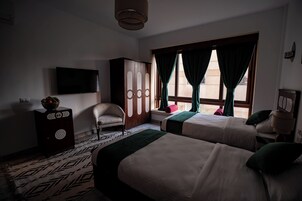 Quarto de hotel com duas camas, uma cadeira, guarda-roupa, televisão e janela com cortinas.
