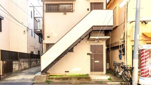 Uma passagem estreita com um edifício bege com uma escadaria que leva a uma porta. Uma bicicleta está estacionada na frente.