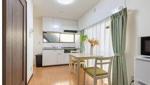 Cozinha compacta com armários brancos, uma mesa de jantar com cadeiras e uma pequena geladeira.