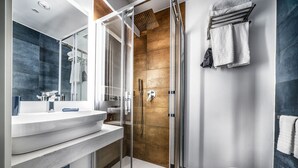 Uma casa de banho moderna com chuveiro em cabine de vidro, lavatório branco e espelho grande.