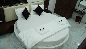 Cama bem arrumada com lençóis brancos e travesseiros pretos, mesa de cabeceira com luminária e uma pequena lixeira.