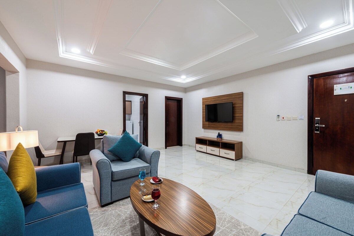Uma sala de estar moderna com um sofá, poltronas, uma mesa de centro, uma TV e um espaço de jantar.