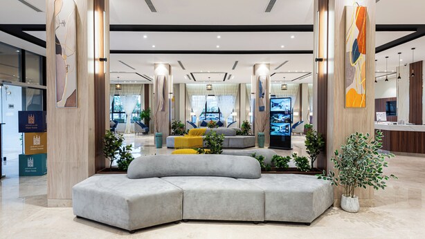 Um lobby moderno com um sofá seccional cinza, uma grande obra de arte abstrata e plantas em vasos.