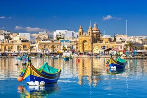 Paisagem urbana à beira-mar, com uma igreja imponente e barcos coloridos em primeiro plano.