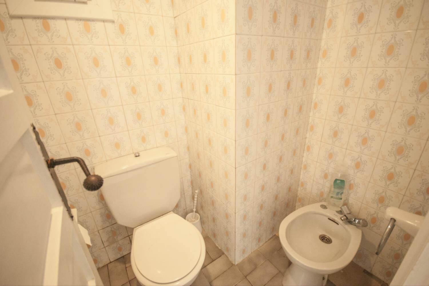 Um banheiro pequeno com vaso sanitário e pia, paredes revestidas com azulejos e área de chuveiro.