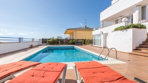 Piscina no terraço com espreguiçadeiras, vista clara da cidade e um edifício moderno ao fundo.