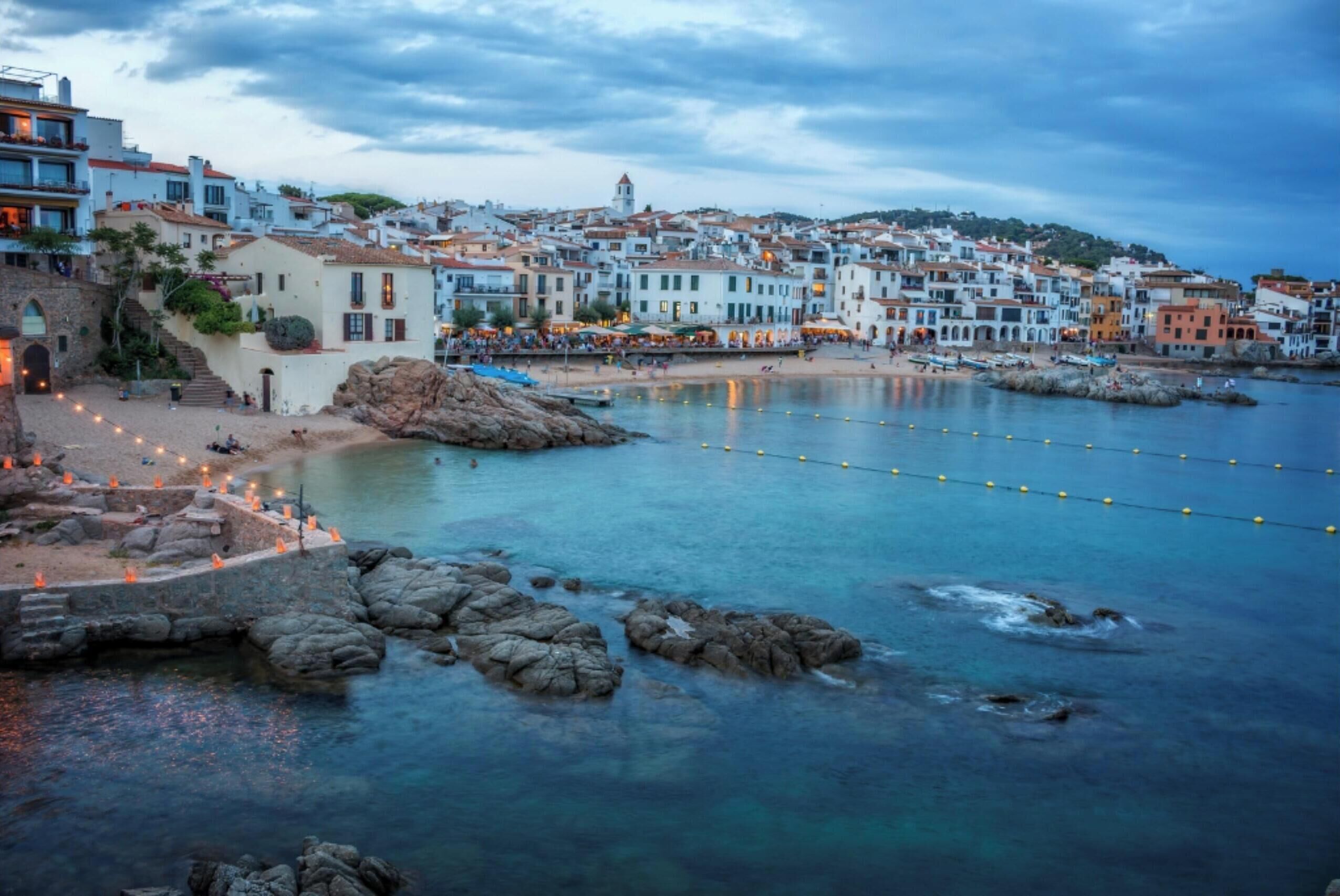 Uma cidade costeira com edifícios históricos, um litoral rochoso e um mar calmo.