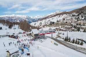 Estância de esqui com teleférico, montanhas cobertas de neve e uma vila ao fundo.