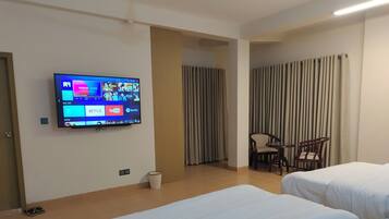 Quarto de hotel com televisão exibindo diversos aplicativos de streaming, duas camas, uma mesinha com cadeiras e uma cortina.