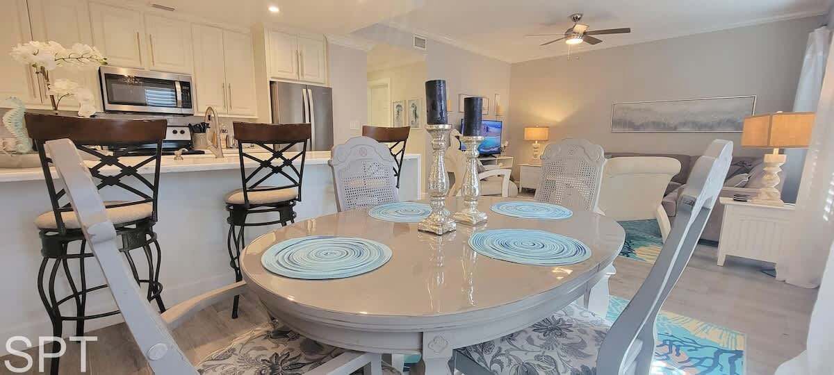 Uma área de refeições com uma mesa redonda, cadeiras e uma cozinha ao fundo.