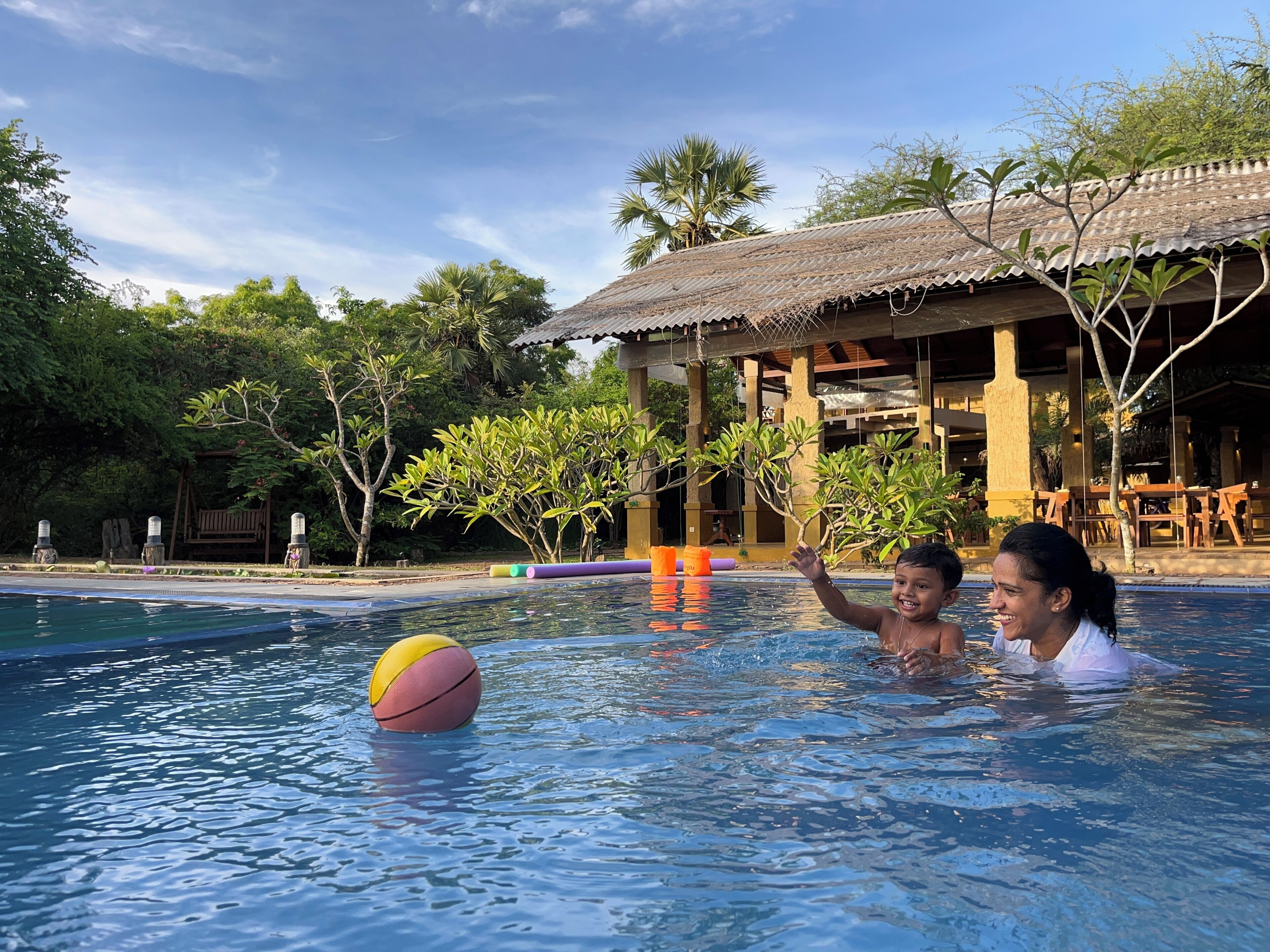 Piscina com uma boia de praia, cercada por árvores e um edifício com telhado em azulejos.