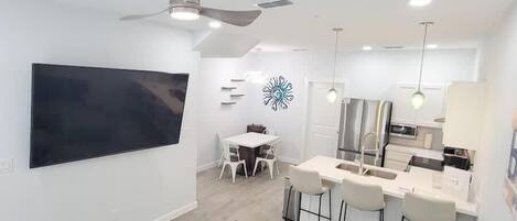 Uma cozinha moderna com armários brancos, uma geladeira de aço inoxidável e um espaço bar com banquetas.