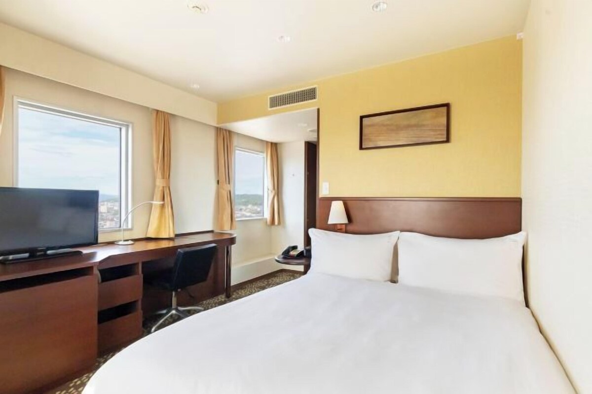Quarto de hotel com uma cama grande, uma escrivaninha com televisão e vista para a cidade.