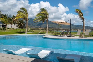 Piscina com espreguiçadeiras e palmeiras, emoldurada por uma paisagem montanhosa.