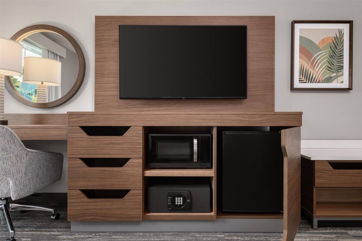 Quarto de hotel moderno com uma escrivaninha de madeira, televisão de tela plana, micro-ondas e um cofre.
