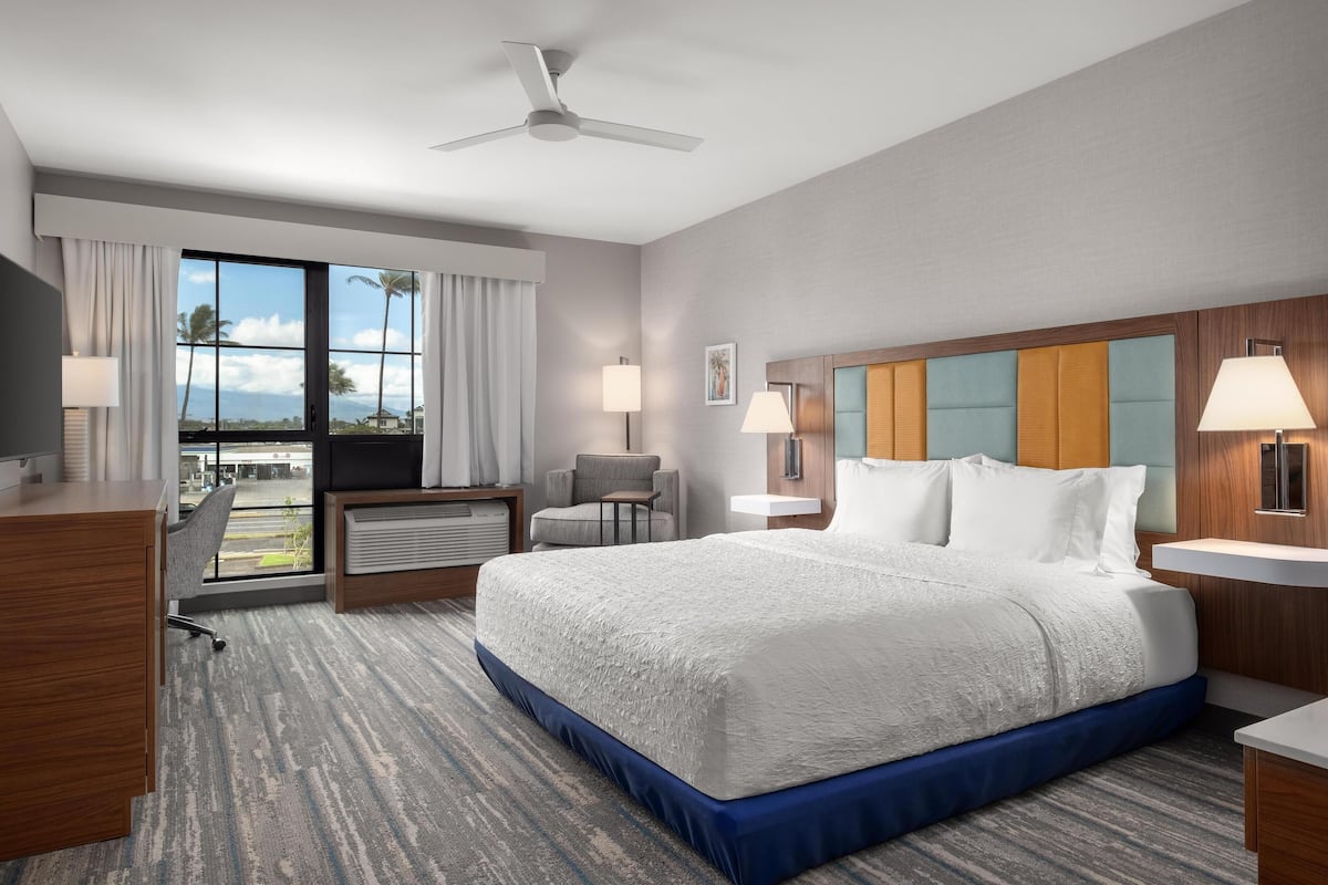 Quarto de hotel com uma cama grande, uma mesa, uma cadeira e vista para o exterior.