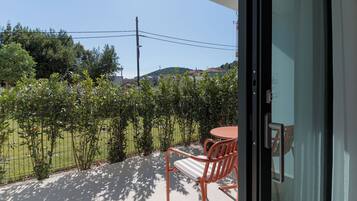 Uma varanda com mesa e cadeiras, vista para uma área verde com árvores e uma colina ao longe.