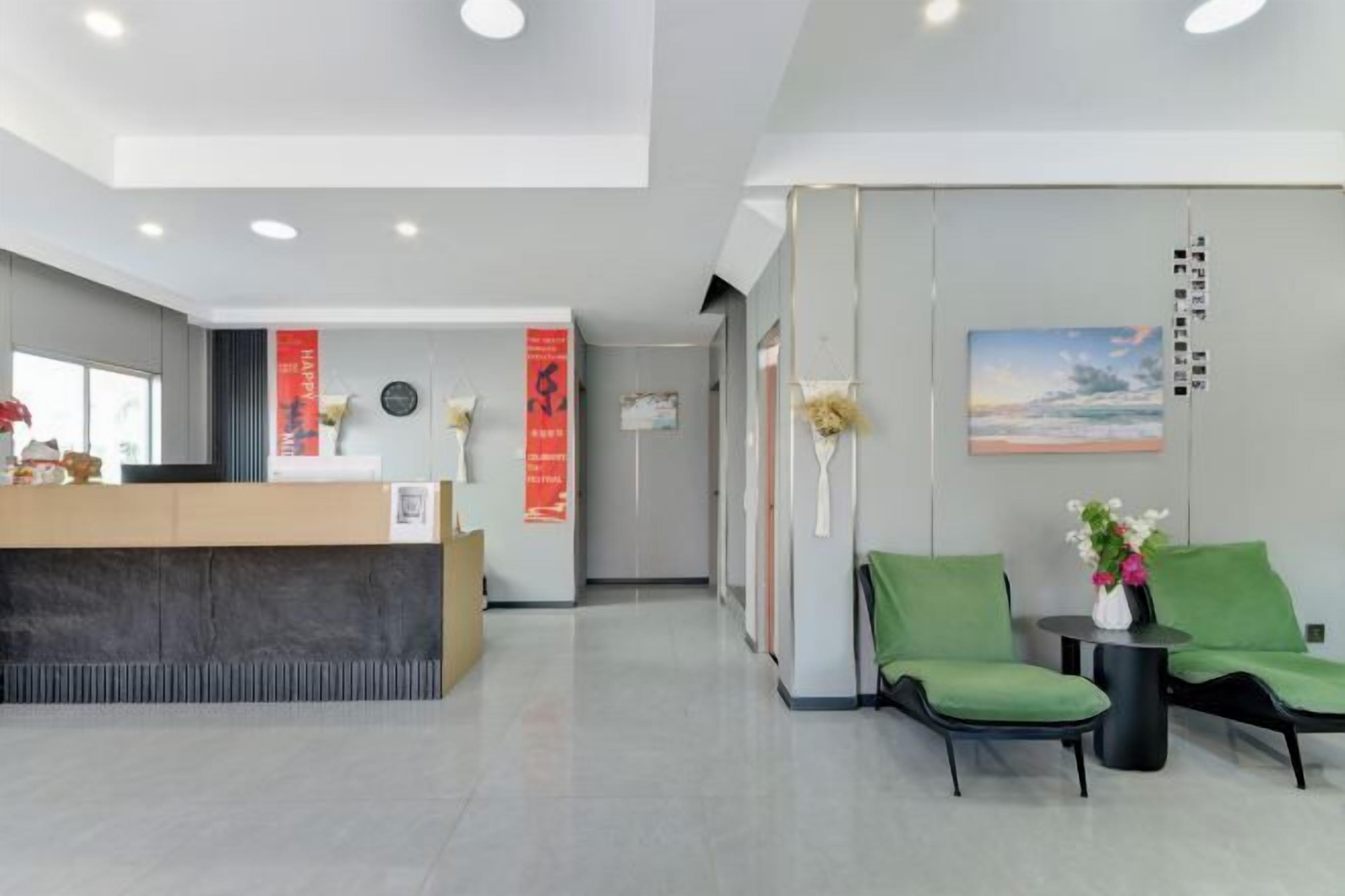 Uma área de recepção com balcão, assentos verdes, um relógio e um quadro na parede.