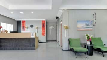 Uma área de recepção com balcão, assentos verdes, um relógio e um quadro na parede.
