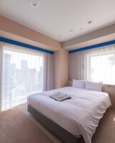 Quarto de hotel com uma cama grande, duas janelas com cortinas leves, vista para a cidade e design moderno.